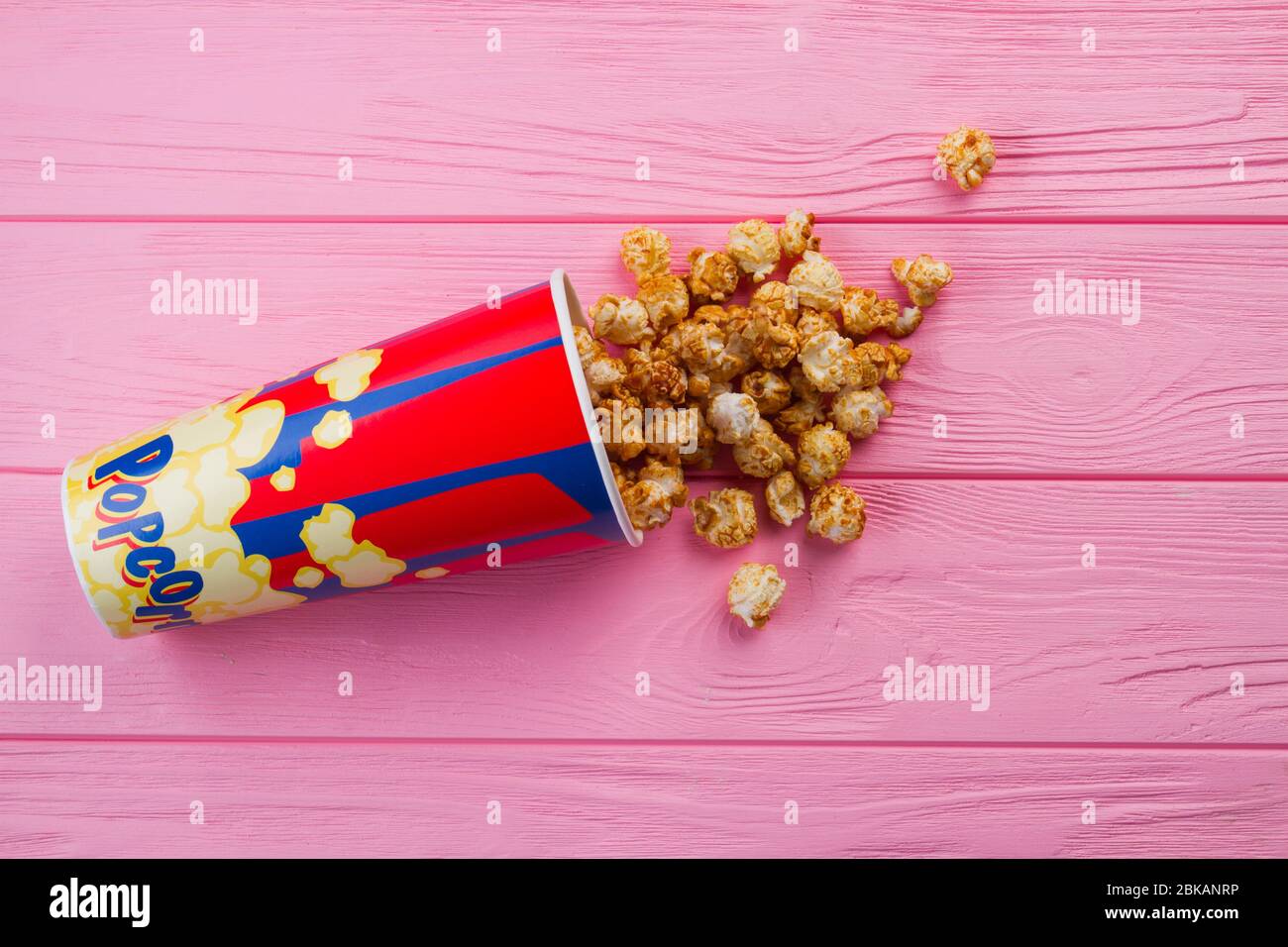 Deep frying popcorn from overturned bucket on pink wooden background ...