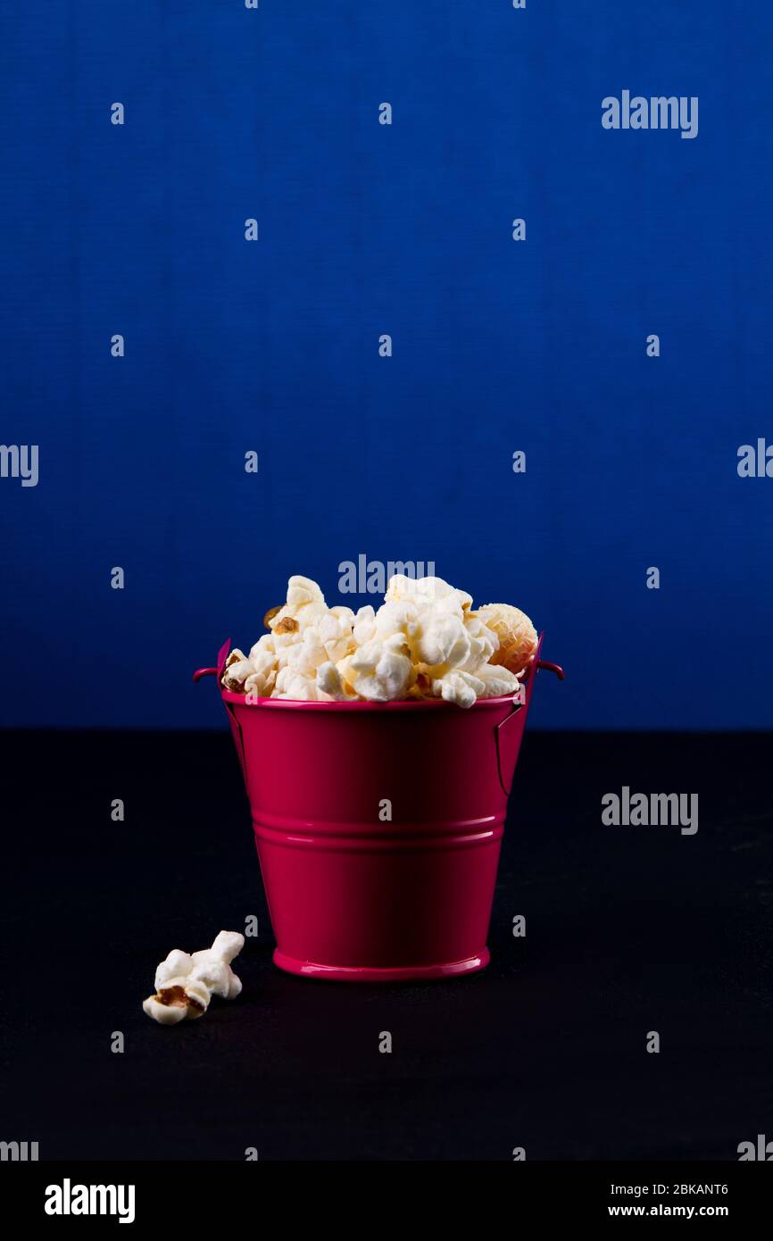 Red bucket full of popcorn on dark blue background Stock Photo - Alamy
