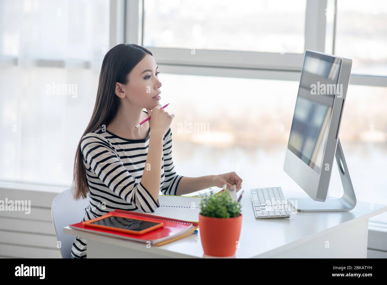 Dark-haired pretty woman in a striped shirt sitting at the computer and ...