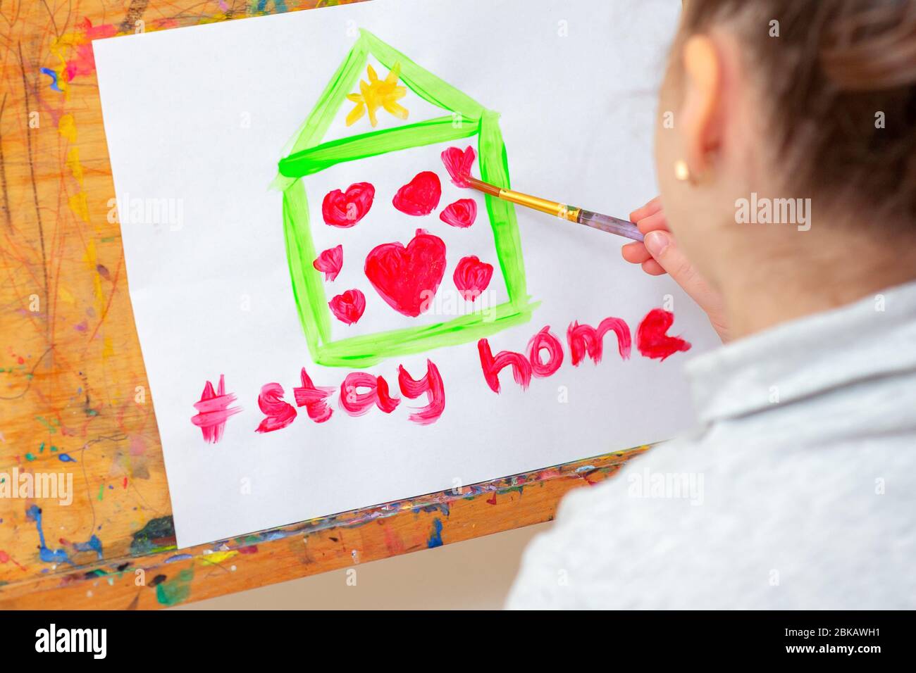 Stay Home concept. Child is drawing house with red hearts on the sheet ...