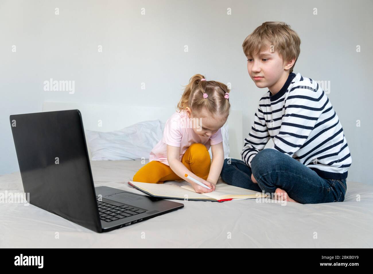 Two kids boy and girl studying at home doing homework using laptop ...