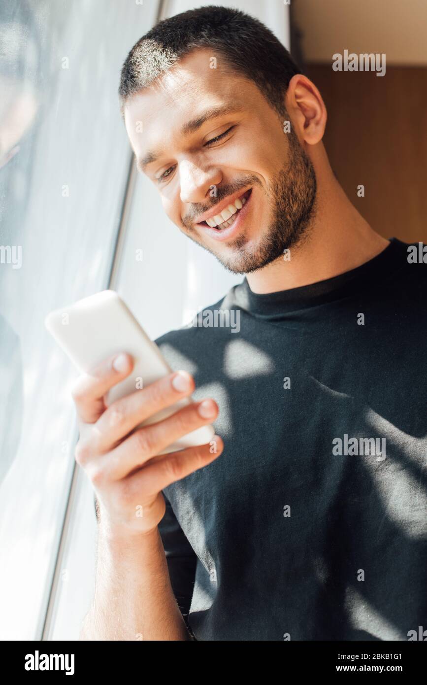 low angle view of happy man using smartphone near window at home Stock ...