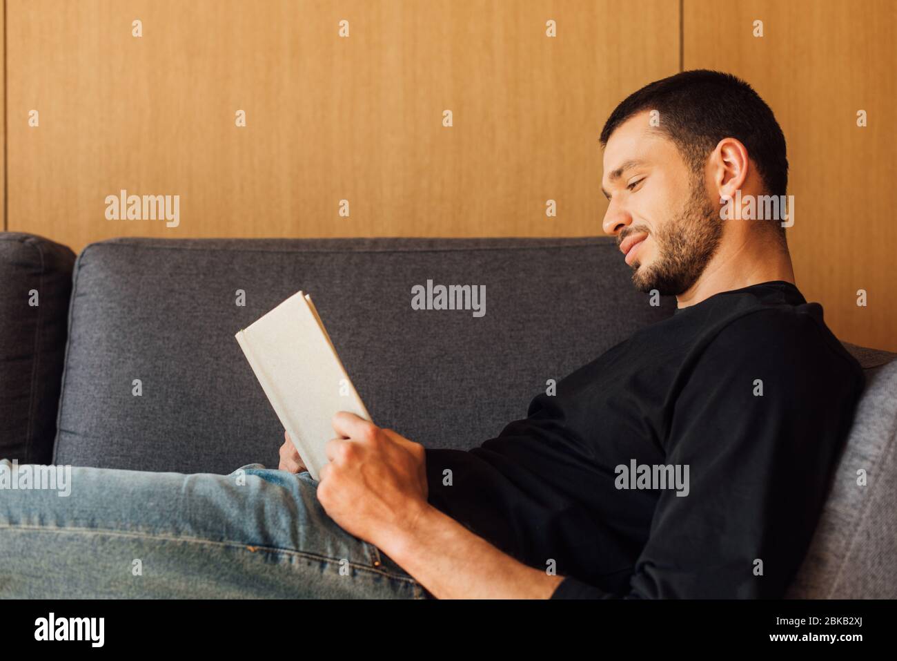 side view of handsome and bearded man reading book in living room Stock ...