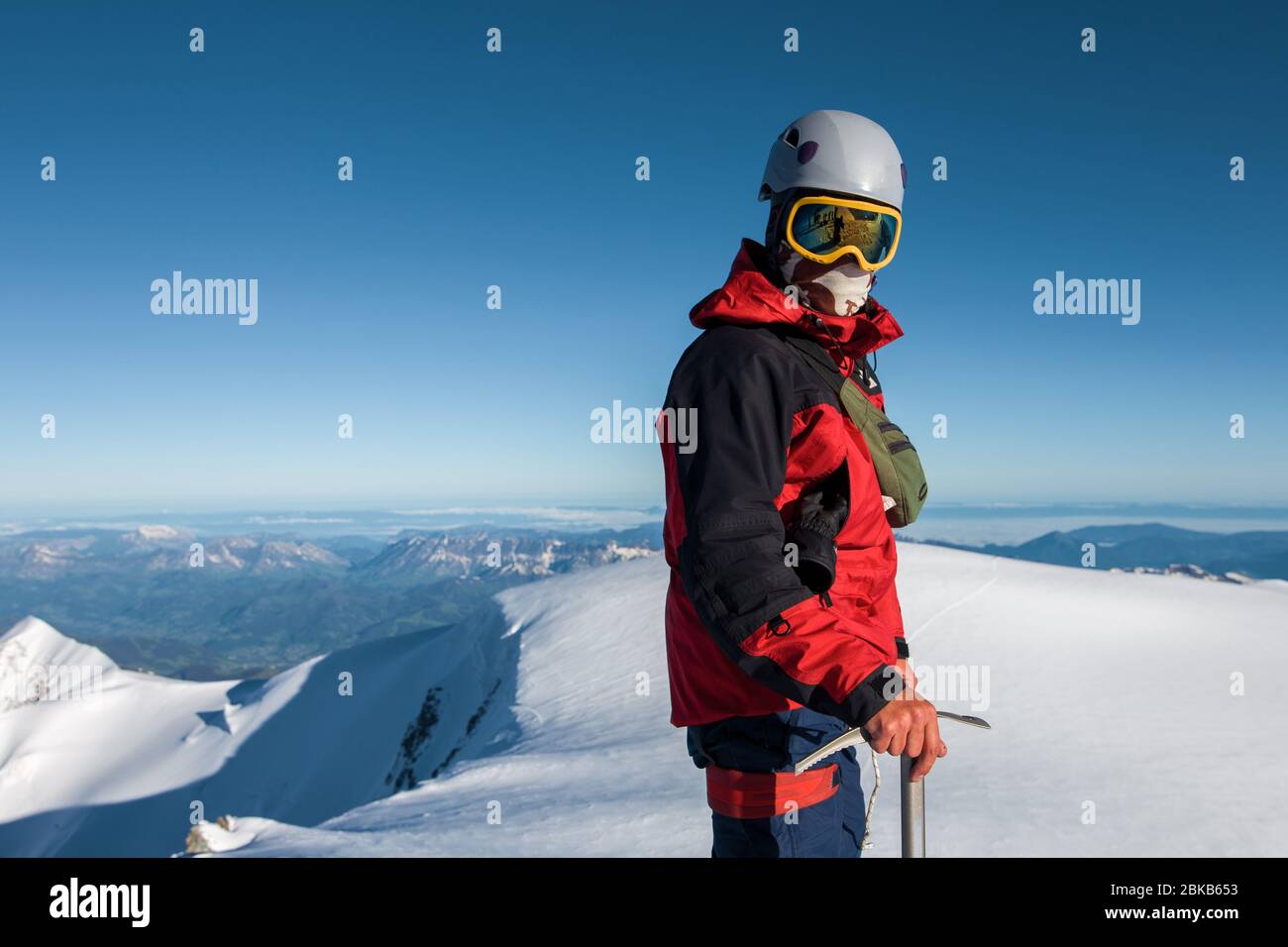 climber in a red jacket stands on top of a mountain against a blue sky ...