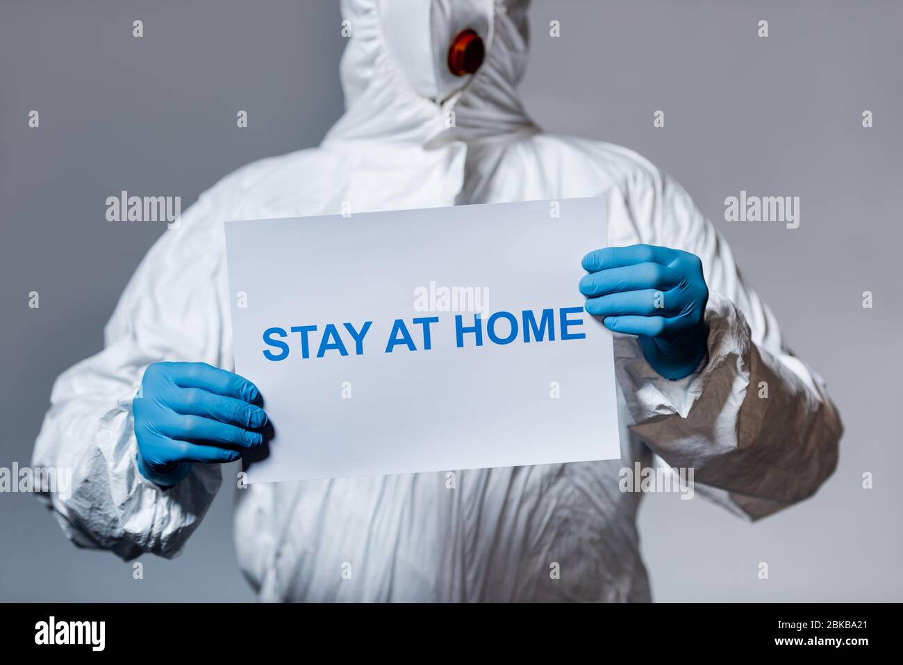 cropped view of man in hazmat suit holding placard with stay at home ...