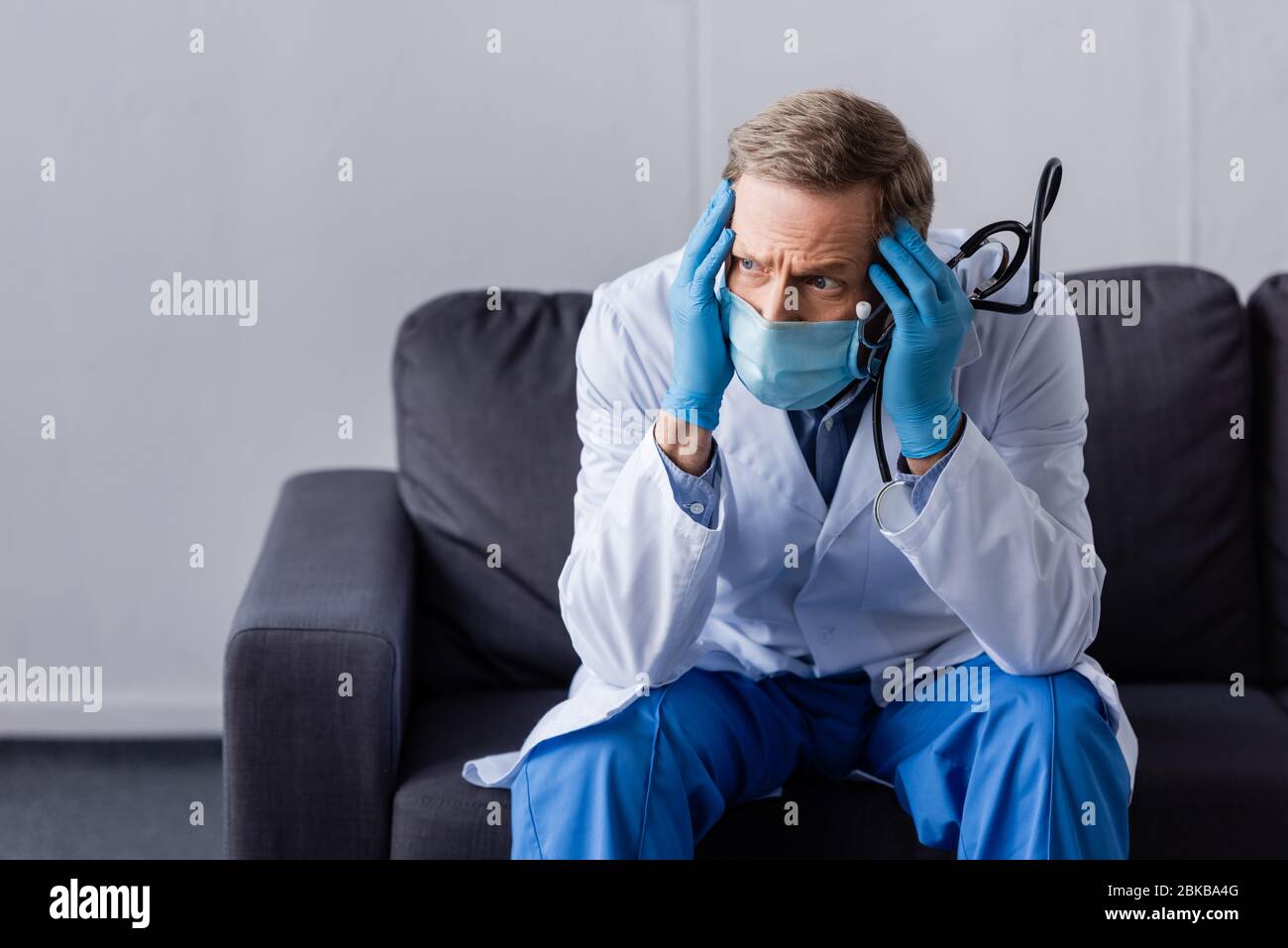 tired mature doctor with headache holding stethoscope while sitting on ...
