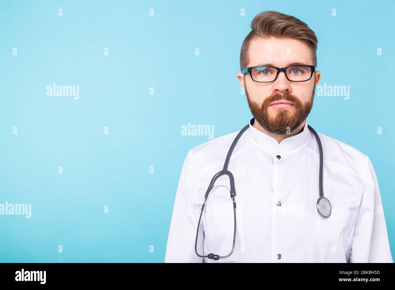 Bearded doctor standing with stethoscope over blue background with copy ...