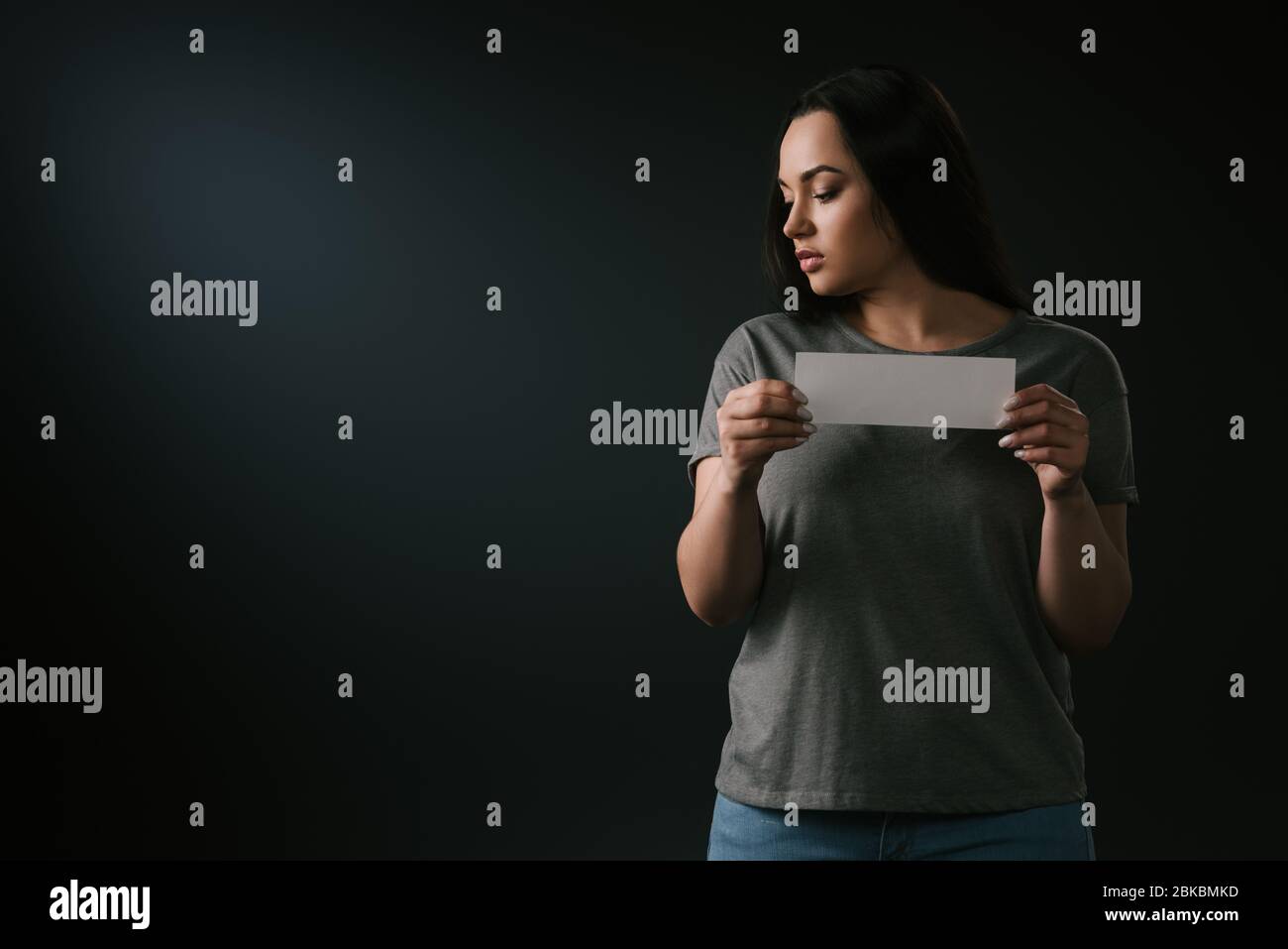 Front view of sad plus size girl holding empty card on black background ...
