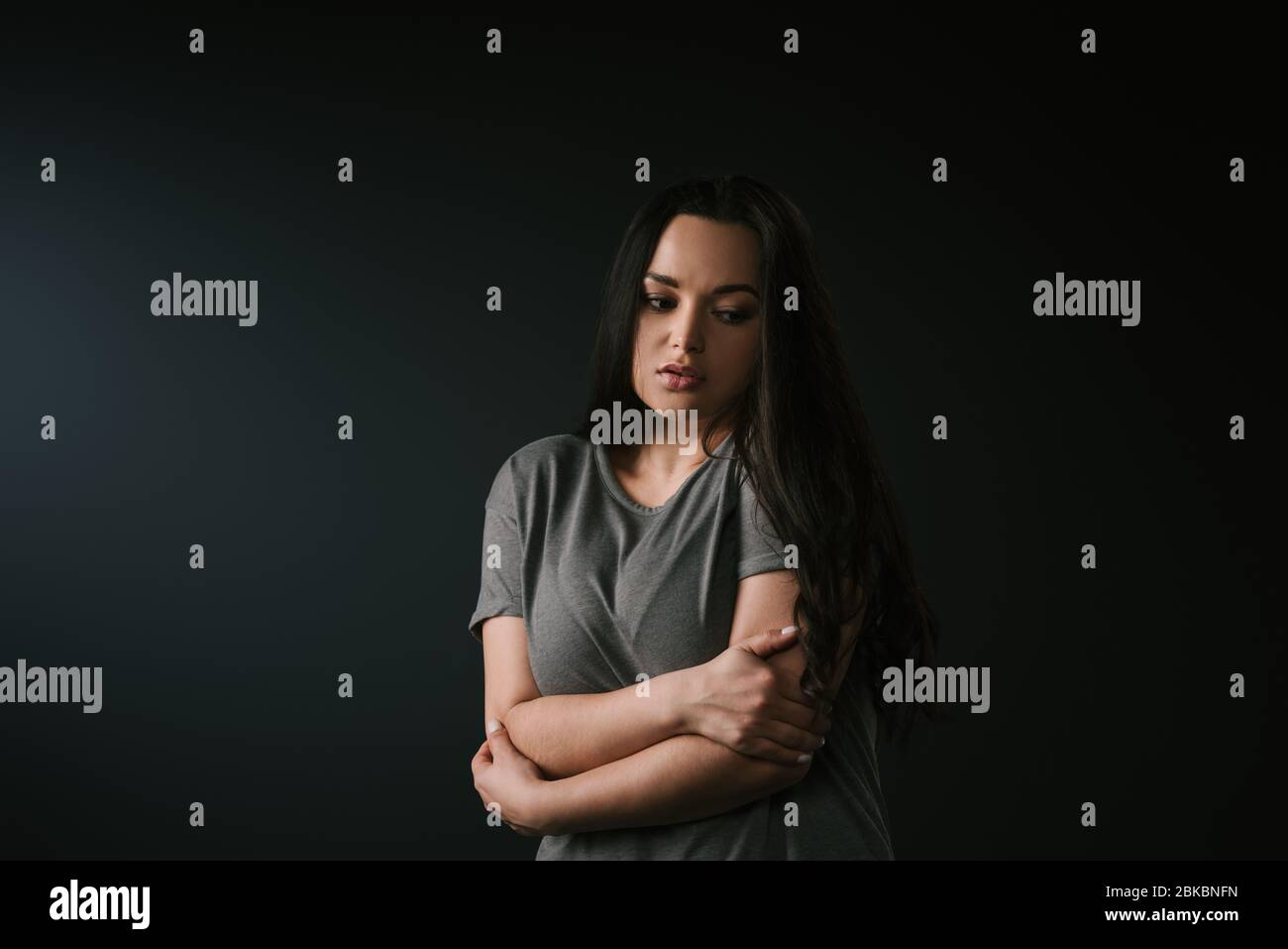 Sad plus size girl hugging herself on black background Stock Photo - Alamy