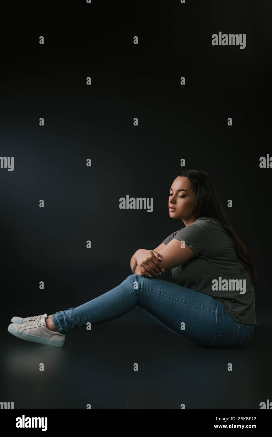 Side view of beautiful sad plus size girl sitting sadly on black ...