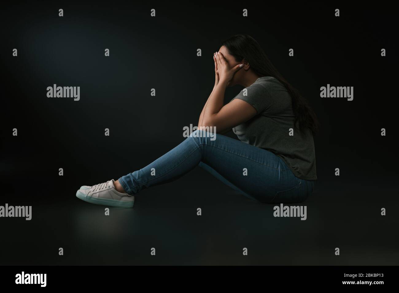 Side view of crying plus size girl covering face with hands and sitting ...