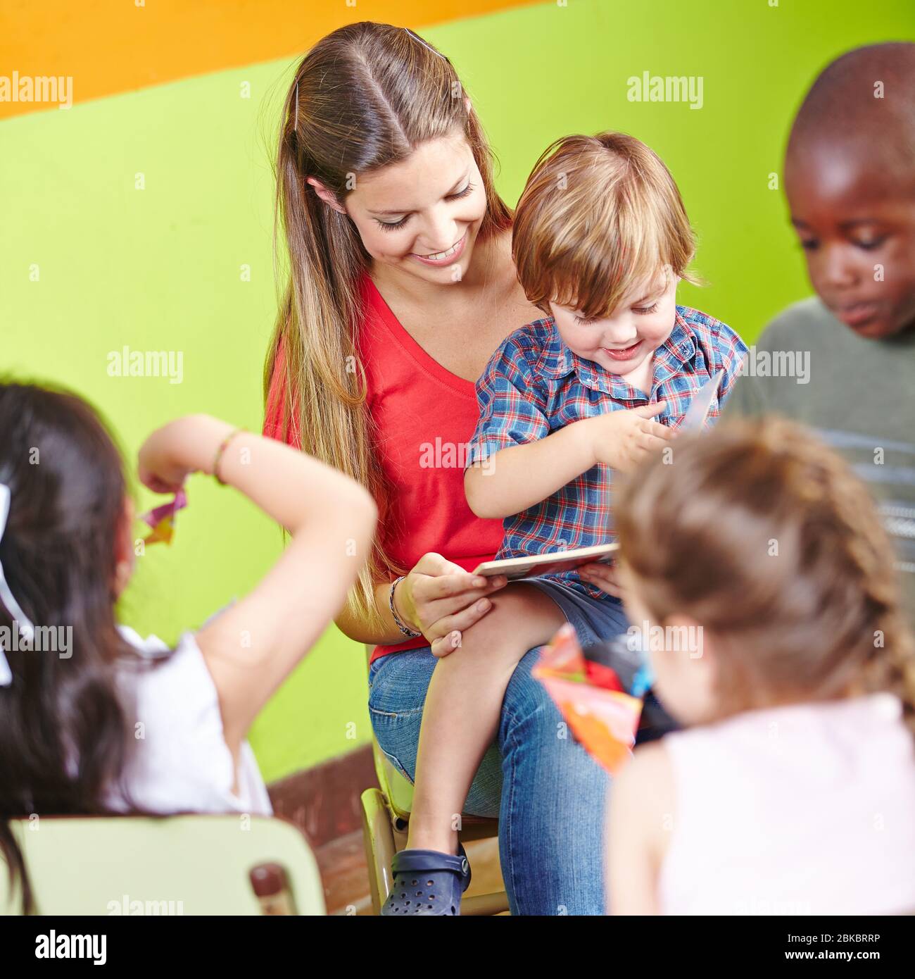 Smiling kindergarten teacher and children read a book together in ...