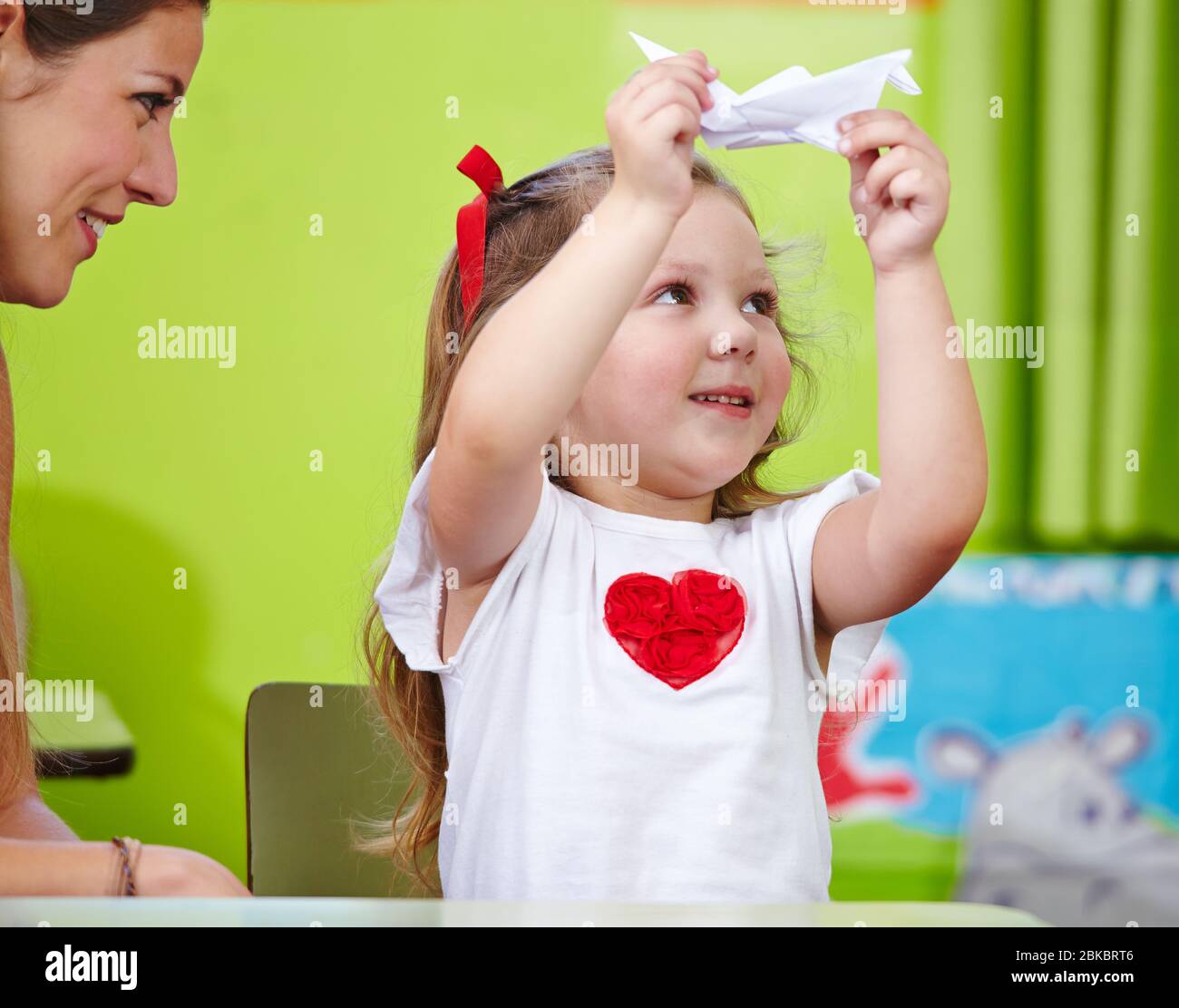 Smiling woman with girl is making origami in the nursery Stock Photo ...