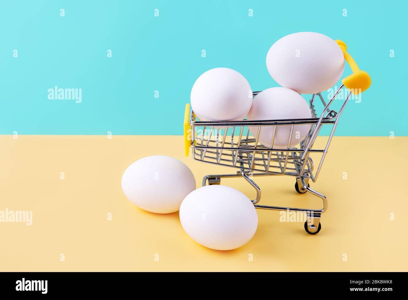 A mini shopping cart with white chicken eggs on a combined yellow-blue ...