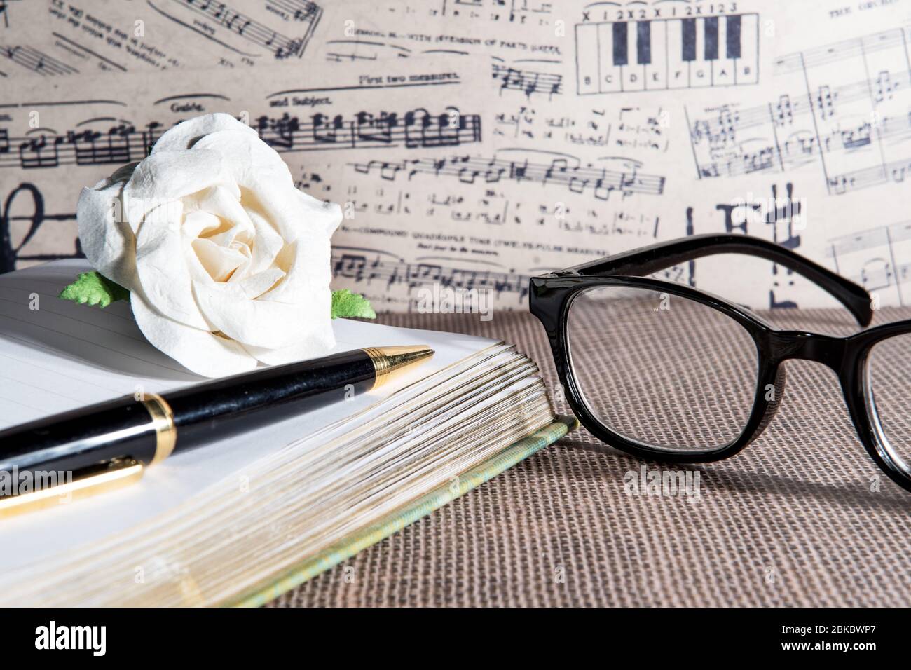 White paper rose on note book with black and gold pen against musical ...