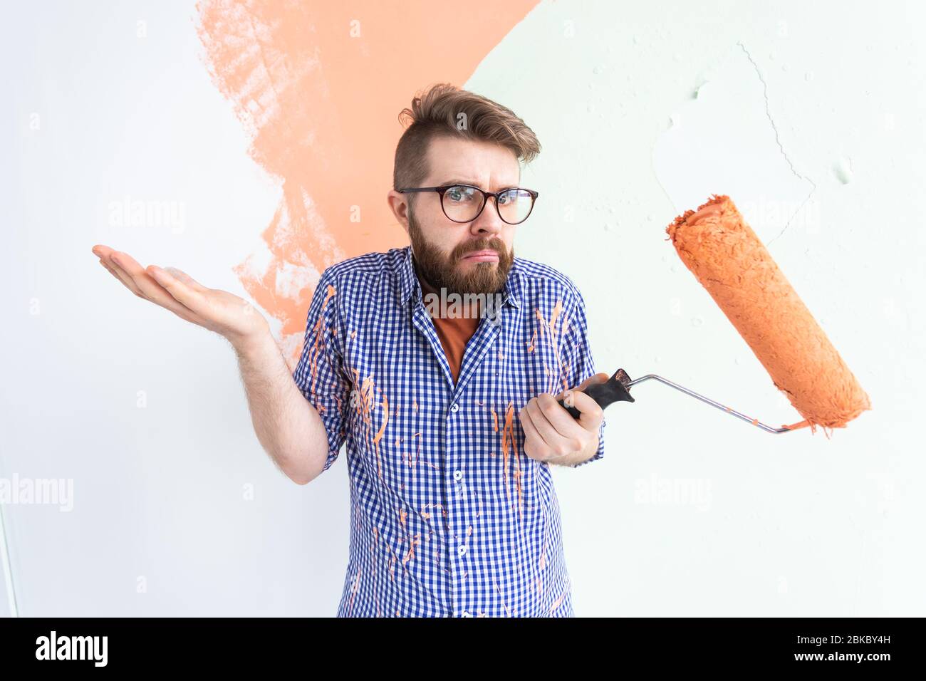Confused male painting the wall with paint roller. Portrait of a funny ...