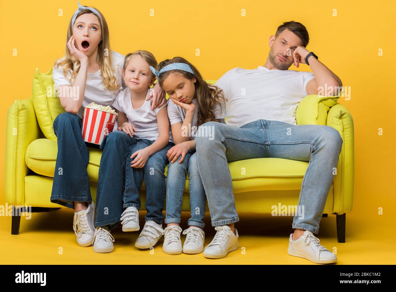 bored parents and kids watching movie on sofa with popcorn bucket on ...