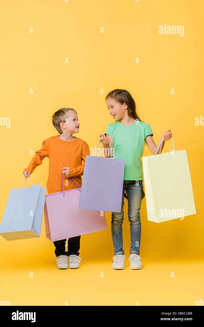 happy kids holding shopping bags and looking at each other on yellow ...