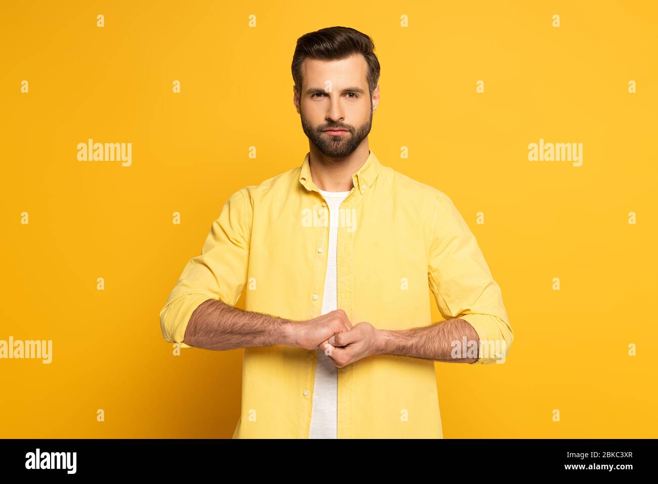 Handsome man showing cohesion sign in deaf and dumb language on yellow ...