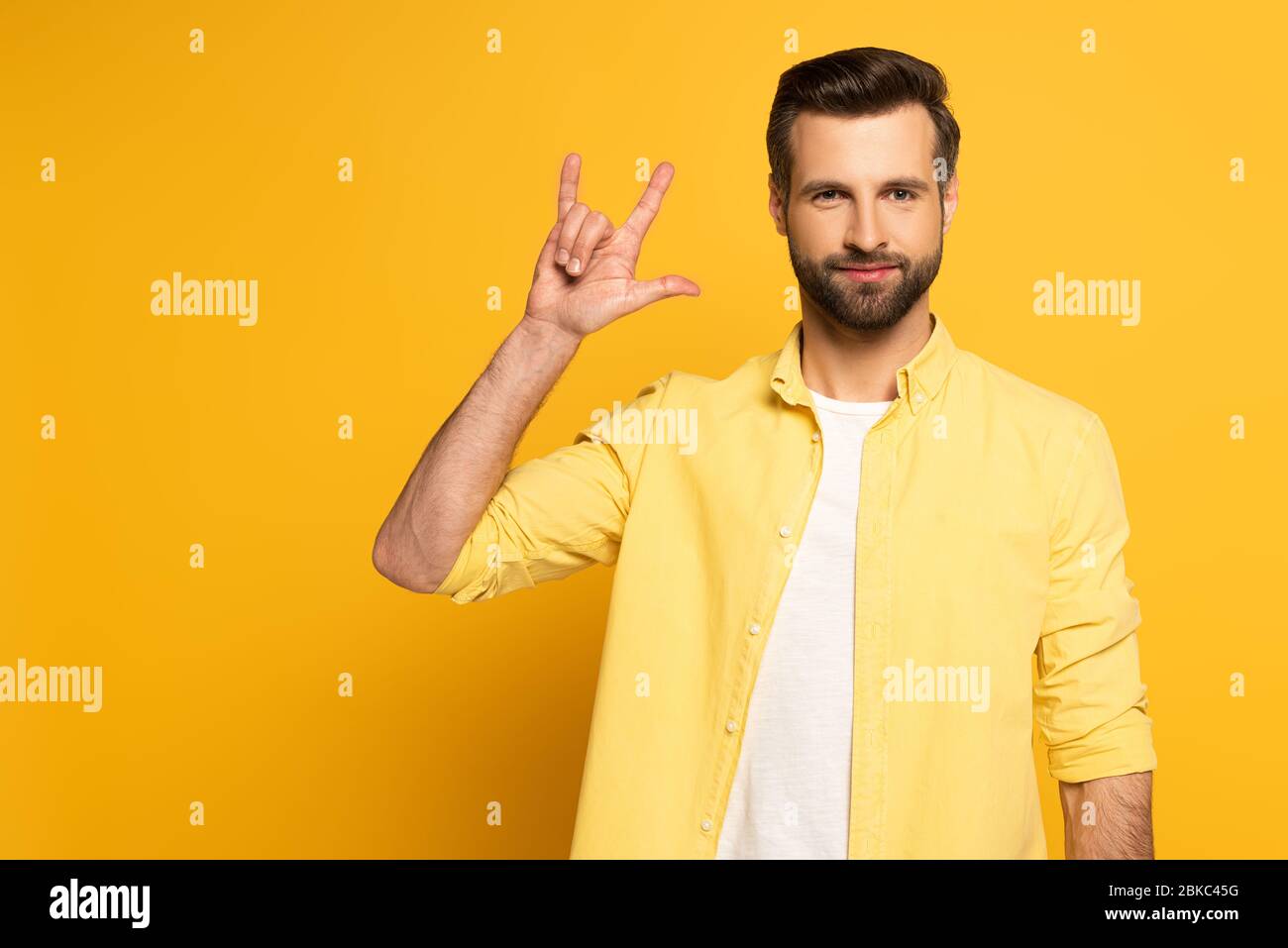 Handsome man showing word love in sign language on yellow background ...