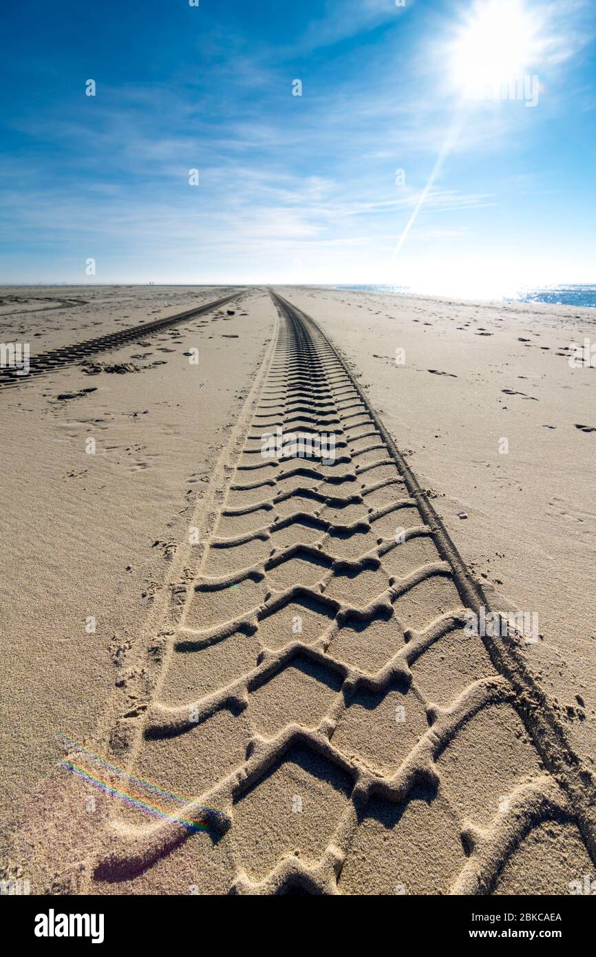 The trail of an off-road vehicle is visible in the sand on the beach in ...