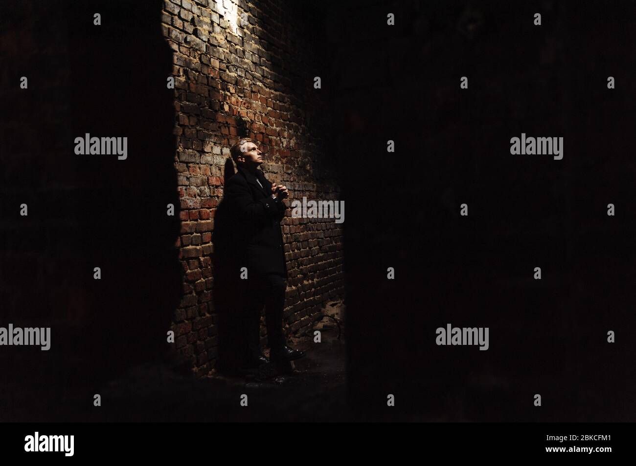 Young man standing near the wall in the abandoned buiding under light ...