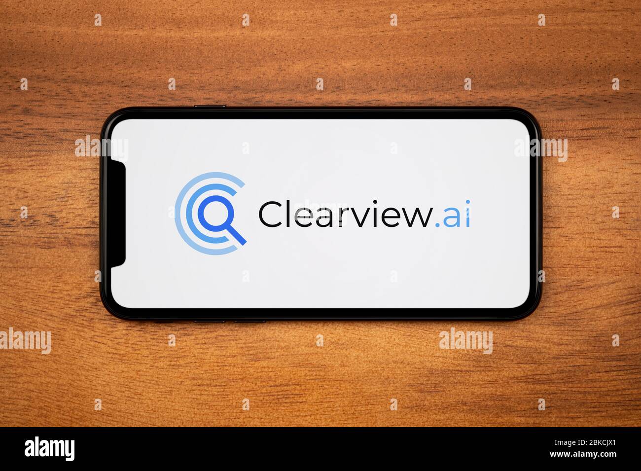A smartphone showing the Clearview.ai logo rests on a plain wooden ...