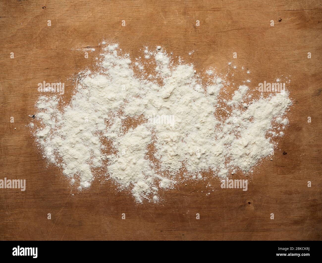 white wheat flour scattered on a brown wooden table, top view, kitchen ...