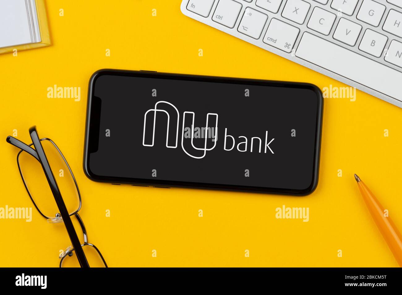 A smartphone showing the Nu Bank logo rests on a yellow background ...