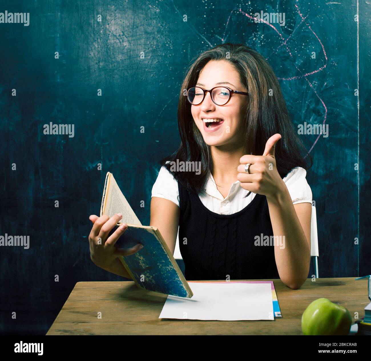 portrait of happy cute student with book in classroom near blackboard ...