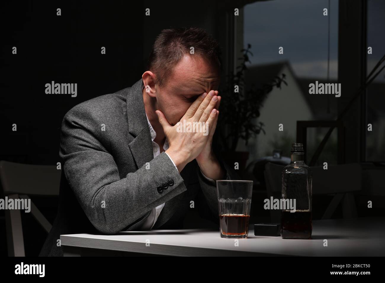 A man with bottle of whiskey on the kitchen. The concept of drunkenness ...