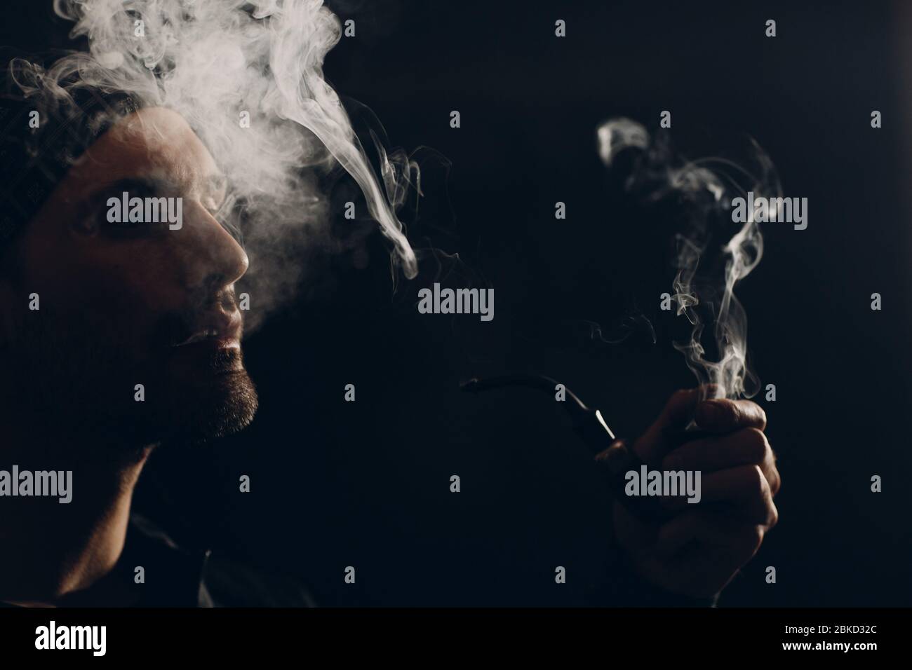 Man smoking a pipe on dark background. Profile portrait with clouds of ...