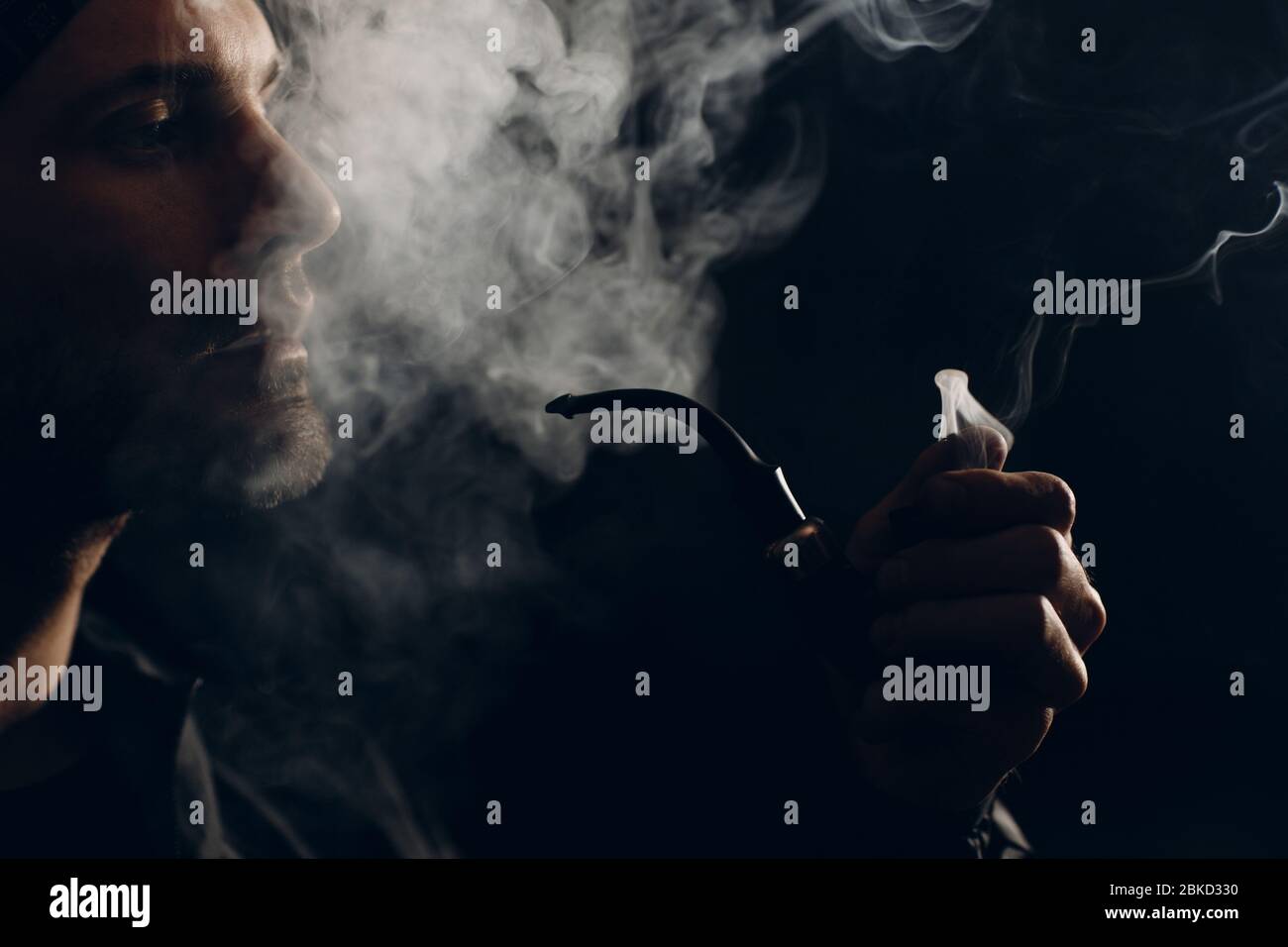 Man smoking a pipe on dark background. Profile portrait with clouds of ...