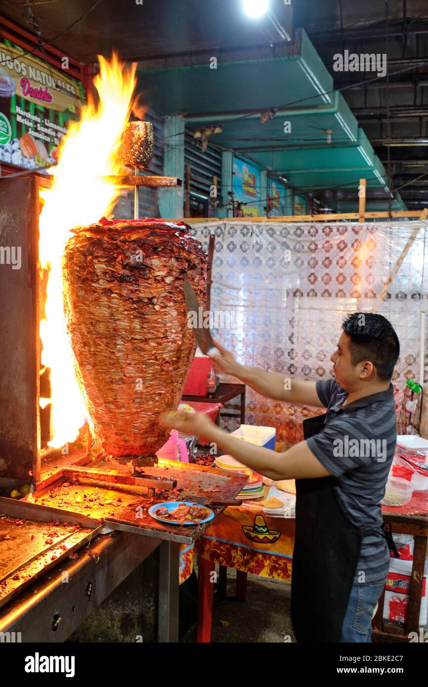 Waiter cutting portions of meat from a large shawarma that is cooking ...