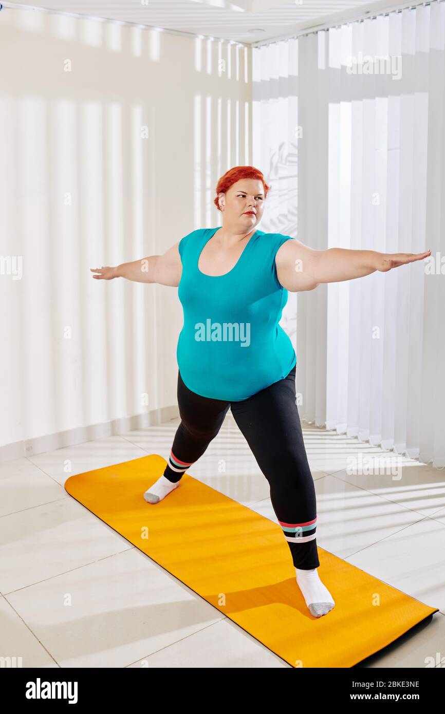 Peaceful focused plus size woman standing in warrior pose when ...