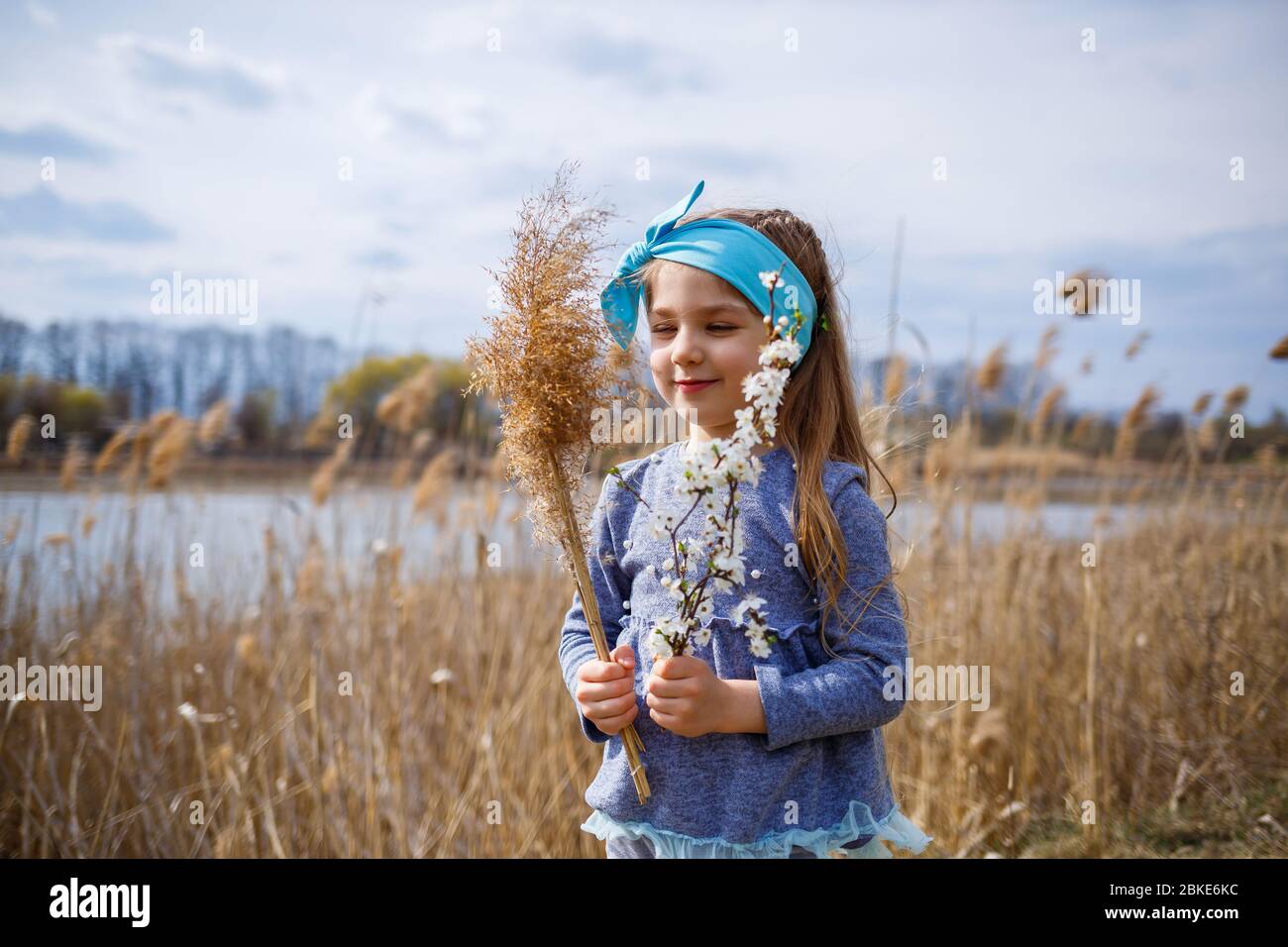 little girl child holds dry reeds and a branch with small white flowers ...