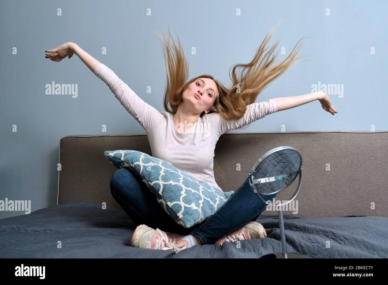 Funny woman with long hair having fun sitting in bed, waving her head ...