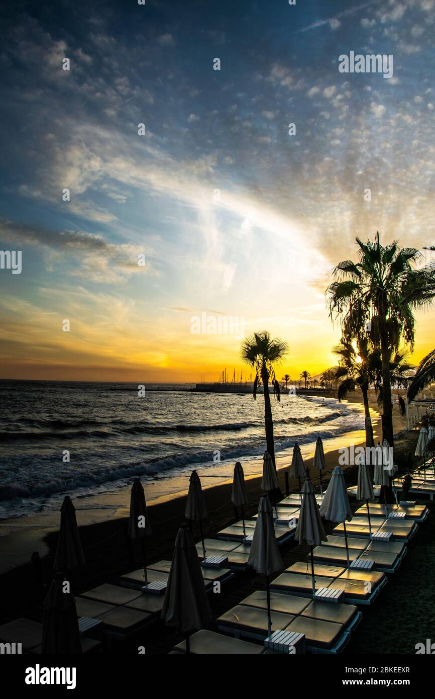 a colourful sunset scene of empty sun loungers on a beach in Marbella ...