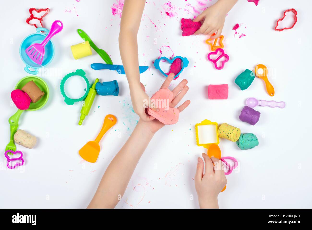 Two little girls play with modeling clay on white background. Top view ...