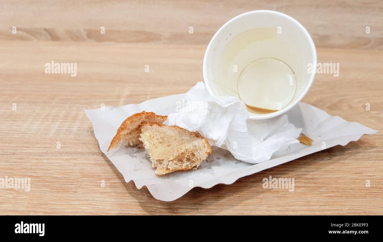 Leftover food on a paper plate and empty dirty paper coffee cup on a ...