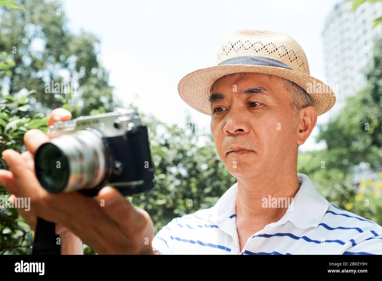 Senior Asian man looking at screen of his digital camera to check ...