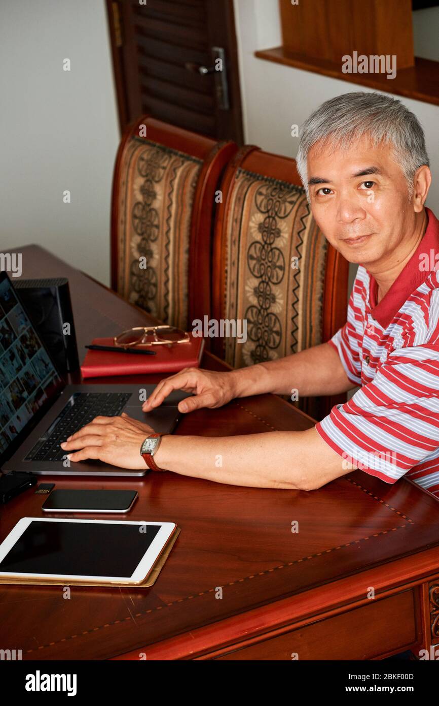 Elderly Chinese man working on laptop at home and editing photos he ...