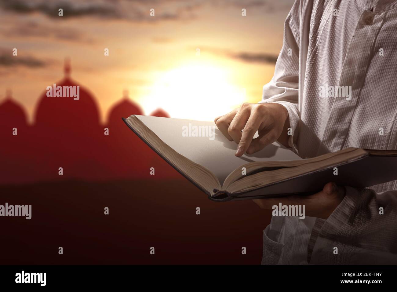Muslim man reading the Quran on his hands with a sunset sky background ...