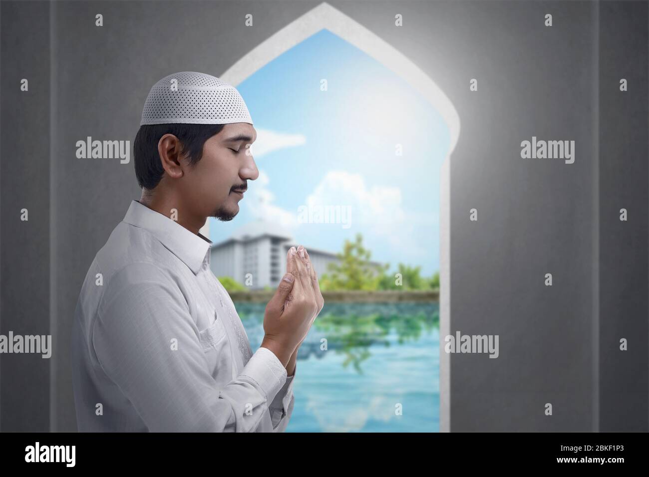 Asian Muslim man standing while raised hands and praying with mosque ...