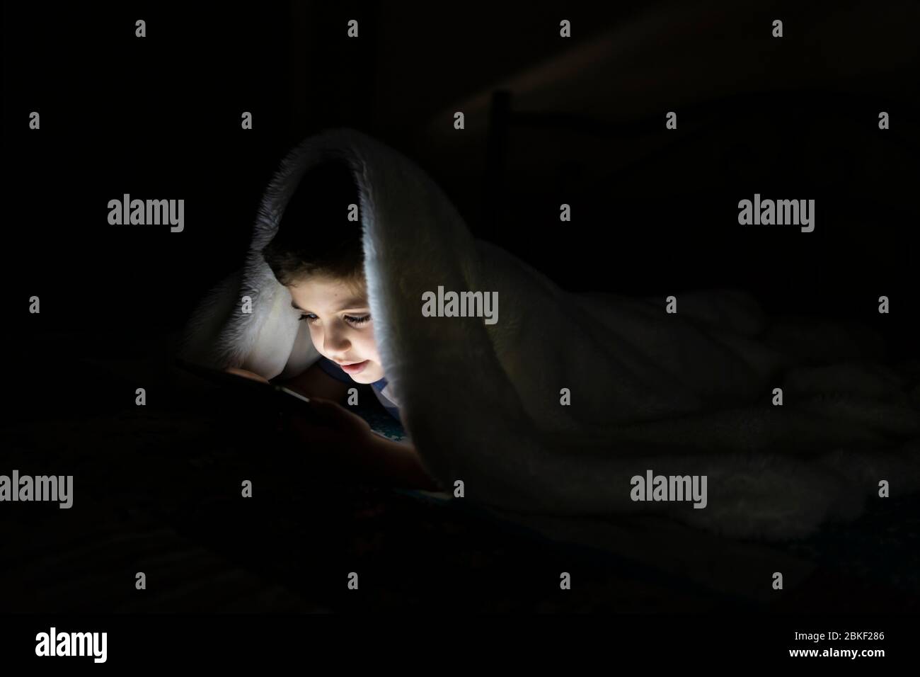 Little child using a tablet covered with a blanket Stock Photo - Alamy