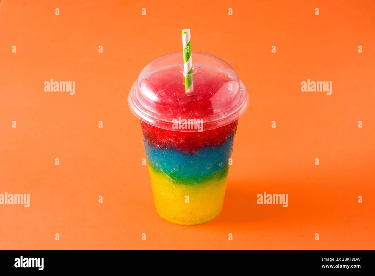 Colorful slushie of differents flavors with straw on orange background ...