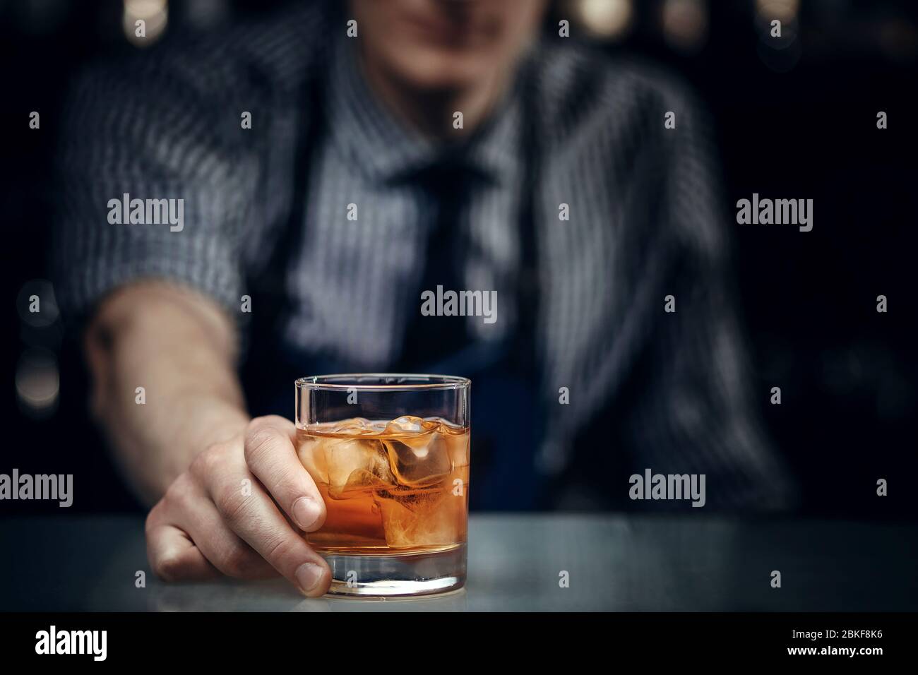 Barman holds out glass of whiskey with ice to male visitor. Concept ...