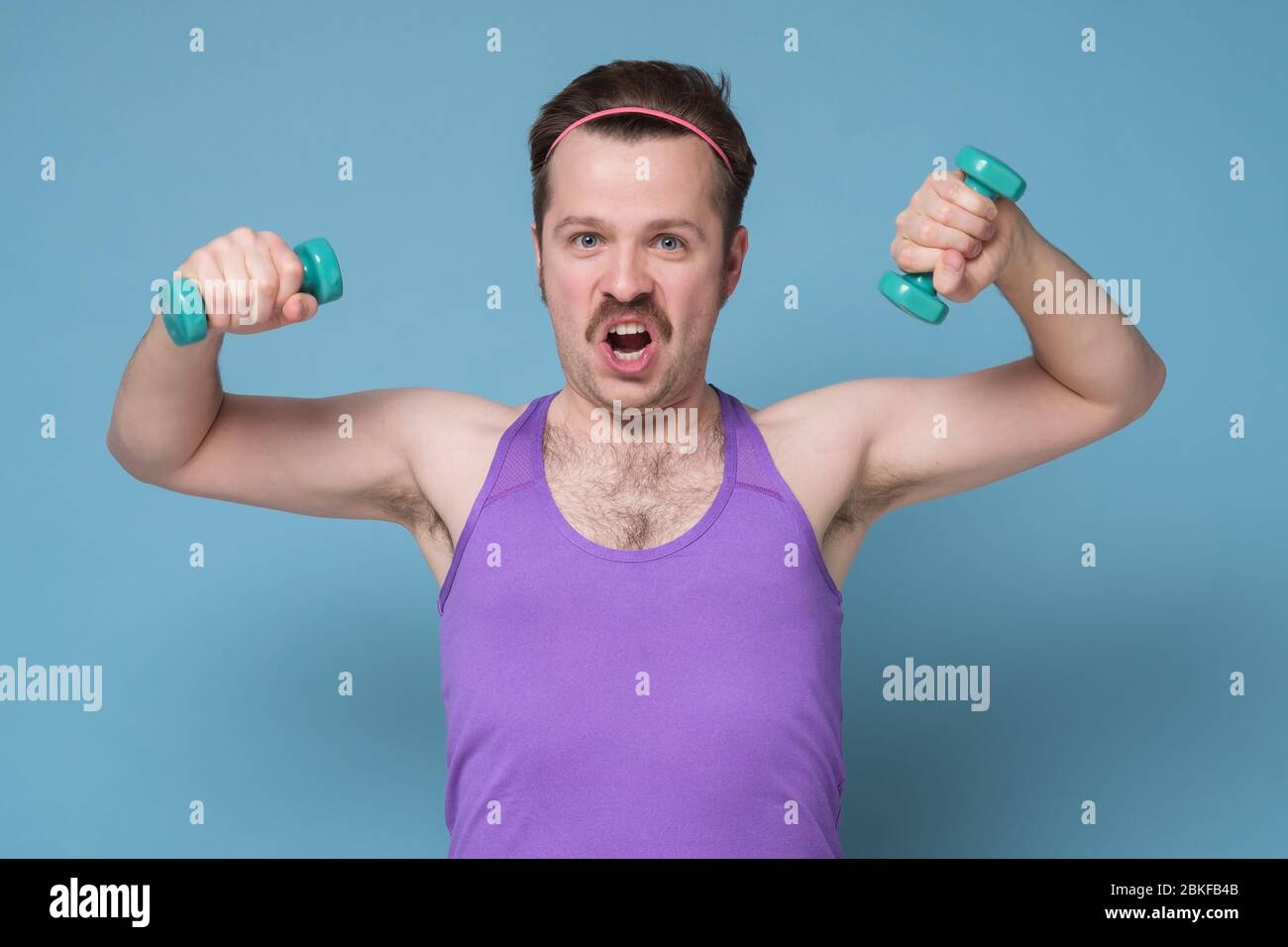 Satisfied young strength man with mustache lifting dumbbell isolated on ...
