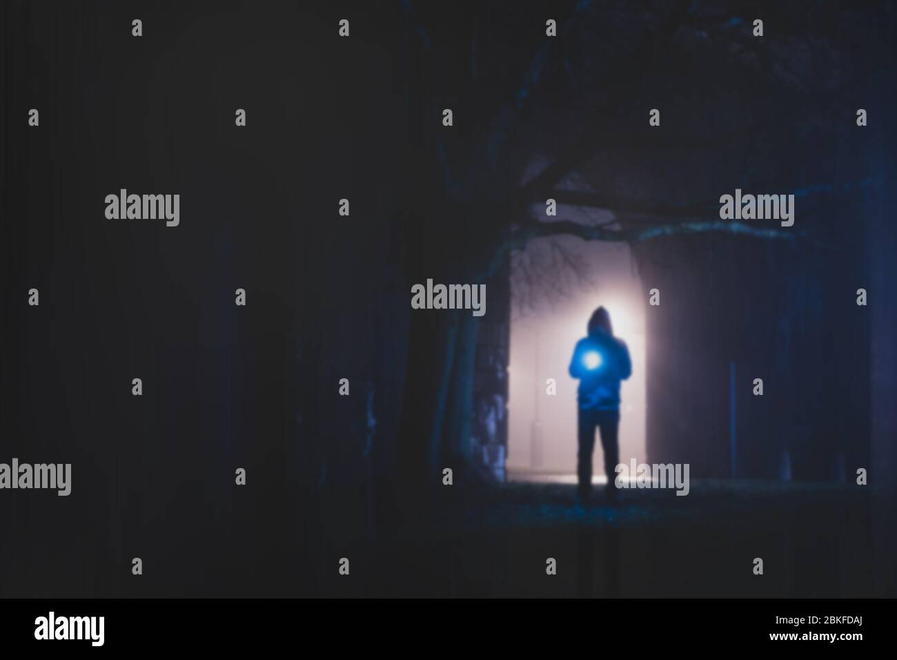 A spooky hooded man holding a glowing light, standing underneath a ...