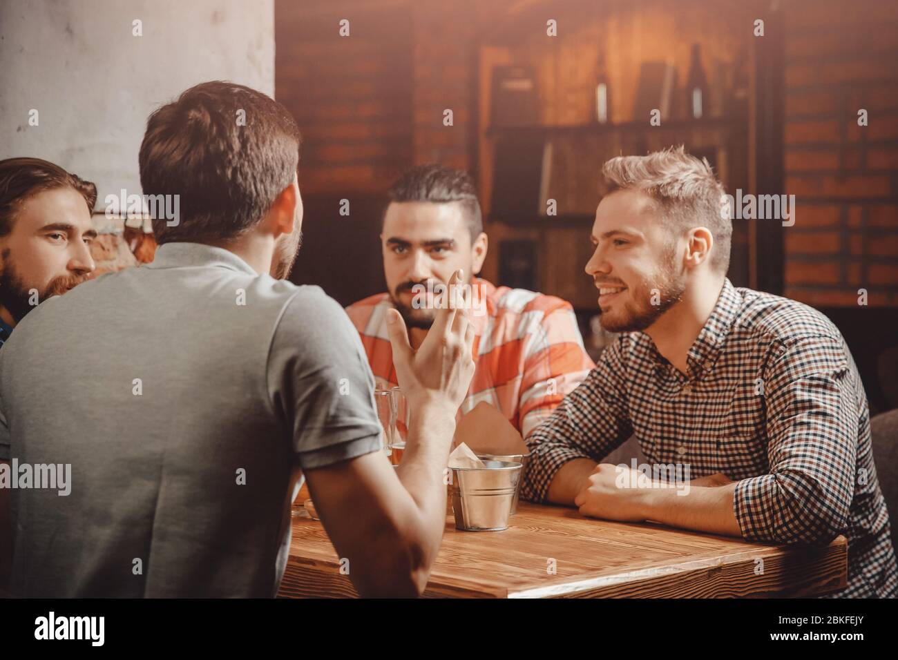 Guy with his back tells cool story. Rest of men sitting at table in ...